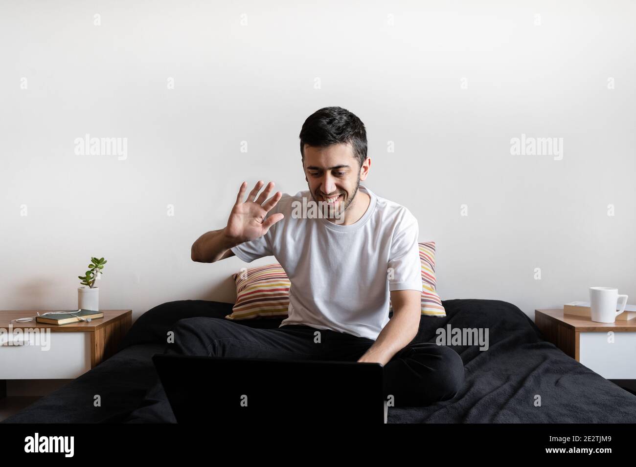 Man waving at the screen of his laptop from his bed - home-office and ...