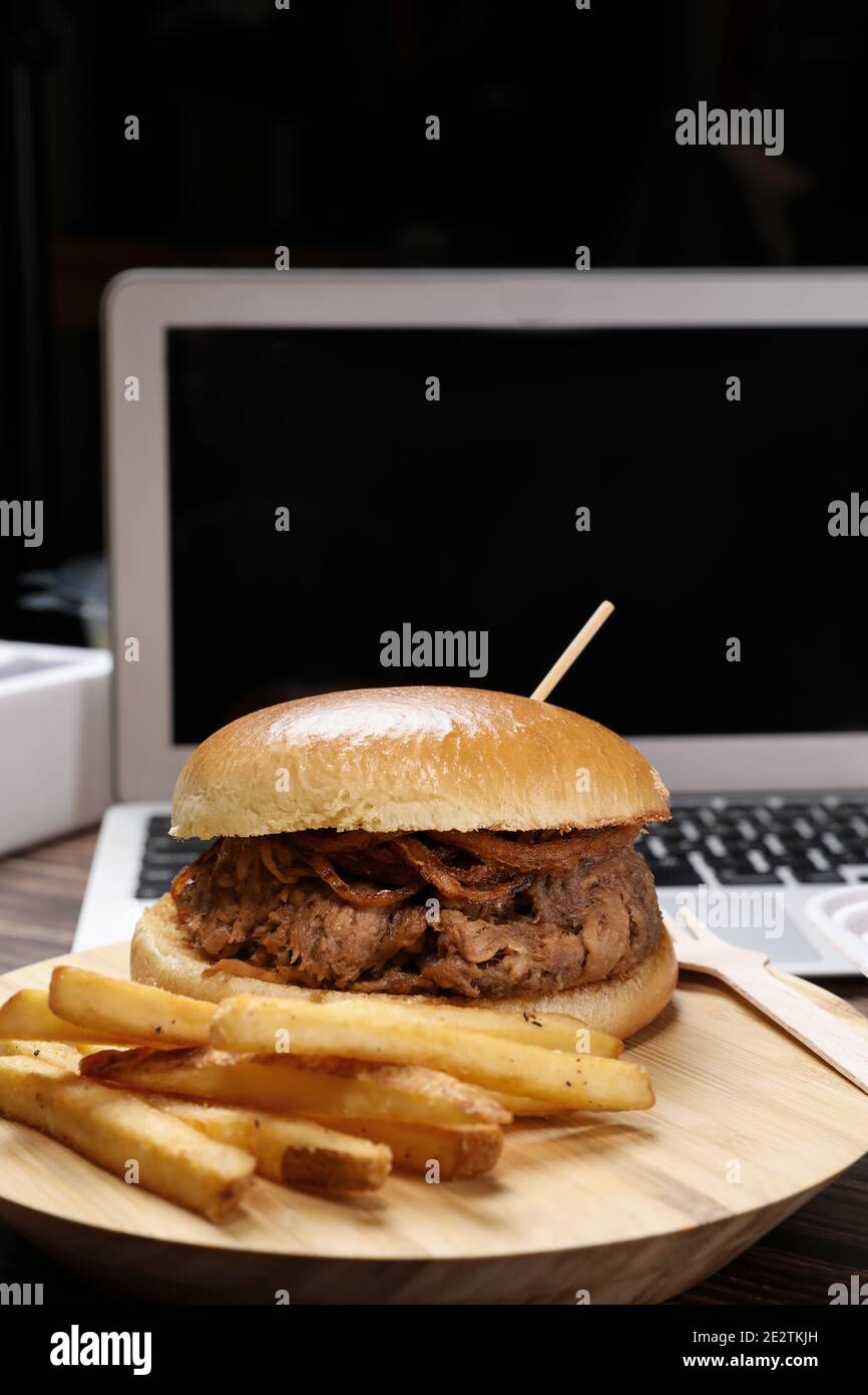 Fresh cooked beef burger with french fries in front of laptop against ...
