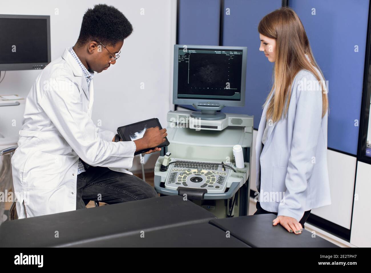 Young male african doctor in modern clinic, holding tablet pc and ...