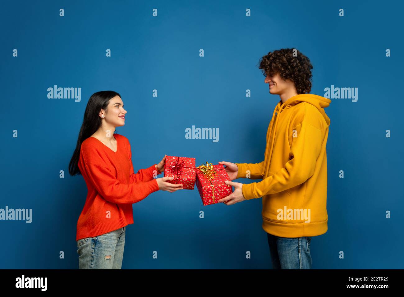 Taking gifts to each other. Beautiful couple in love on blue studio ...
