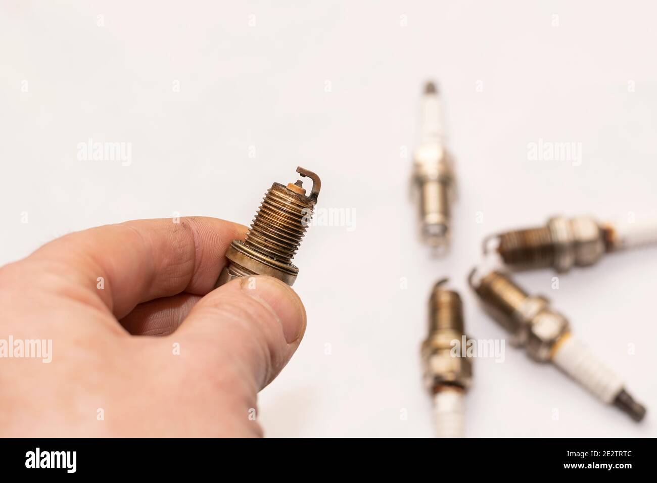 a man's hand holds an old worn out gasoline car spark plug on an empty ...