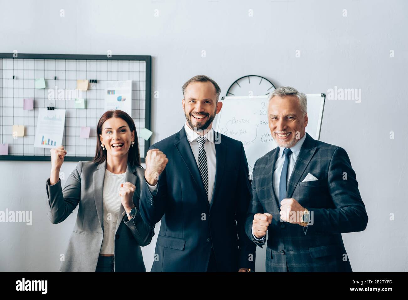 Cheerful businesspeople showing yeah gesture near flipchart in office ...