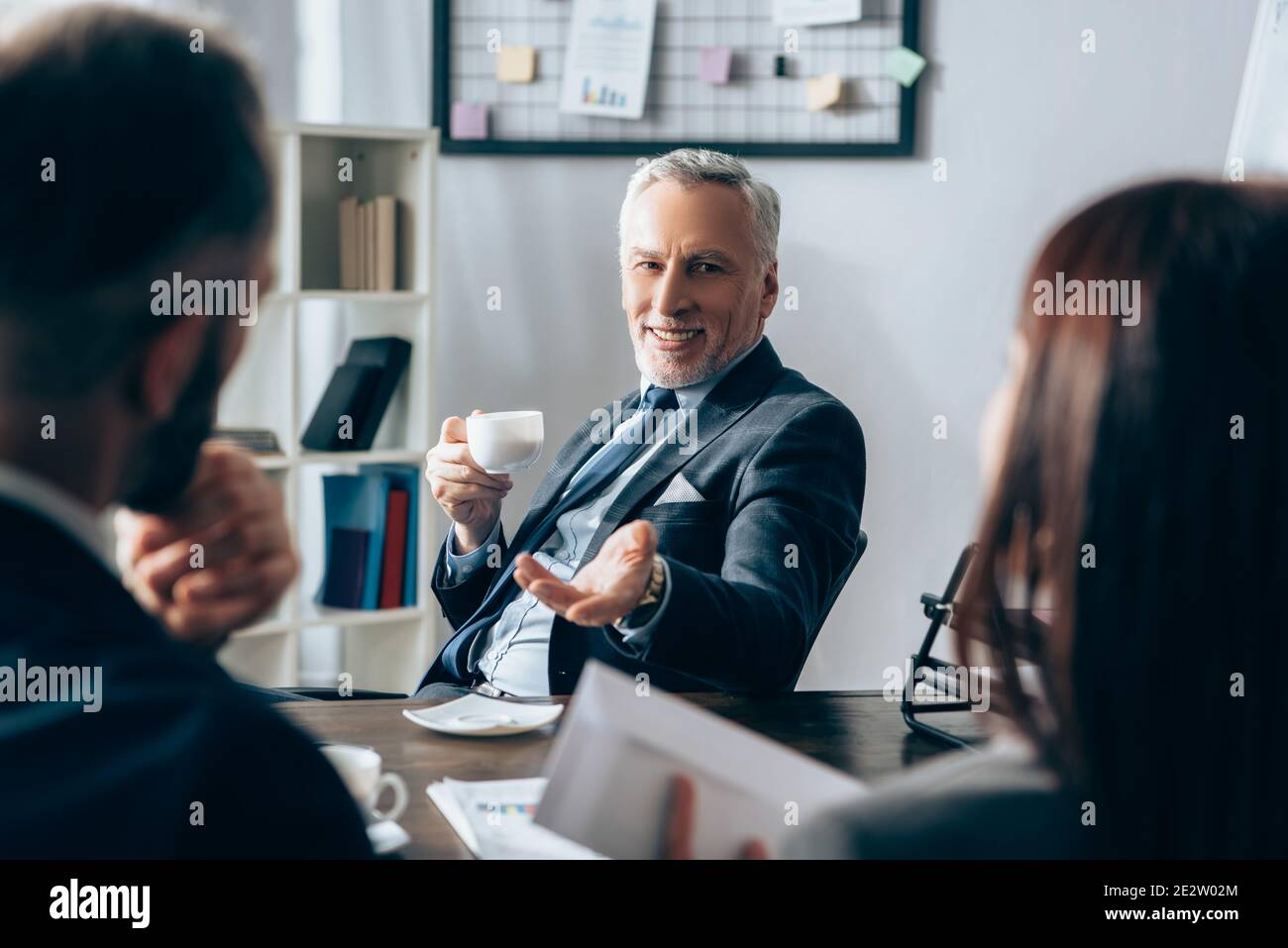 Smiling investor with coffee cup pointing at business people with ...
