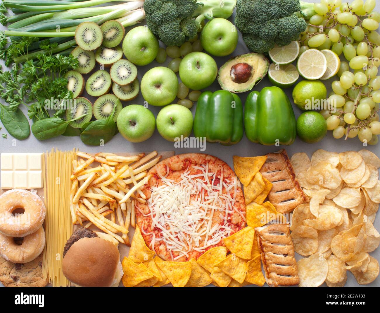 Assorted group of green fruits and vegetables alongside beige junk food ...