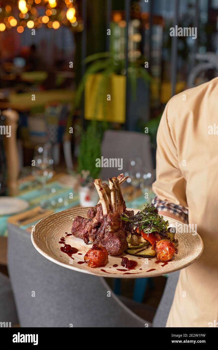 Hands holding cooked Tomahawk long bone ribeye steak on a plate in ...