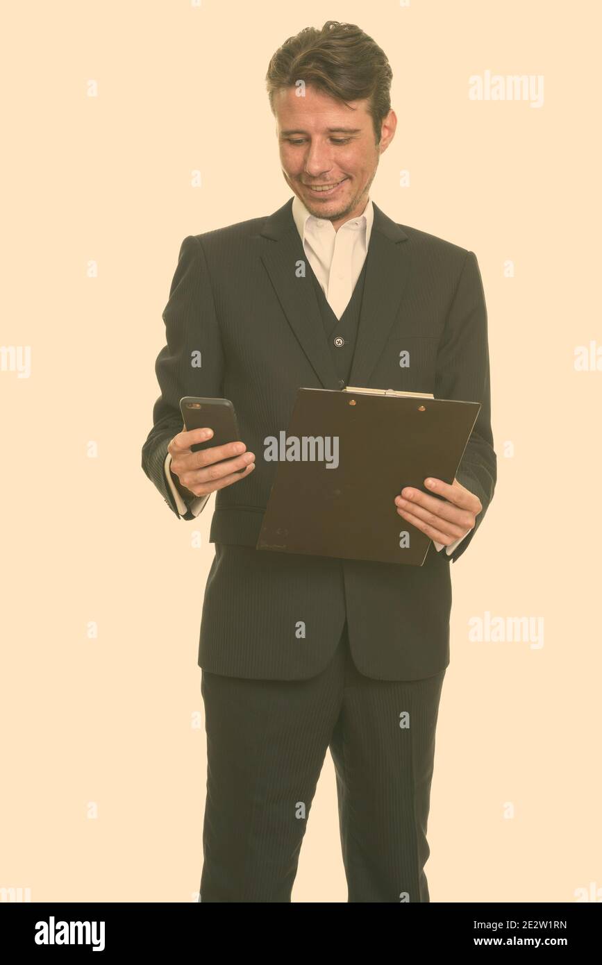 Happy Caucasian businessman using mobile phone while holding clipboard ...