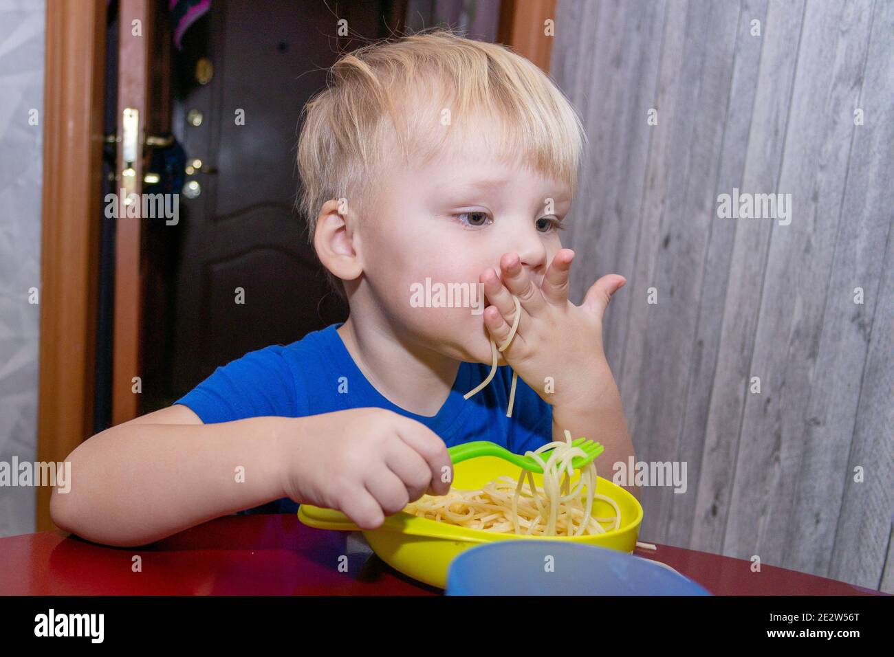 a small child eats noodles in the kitchen, helping himself with his ...