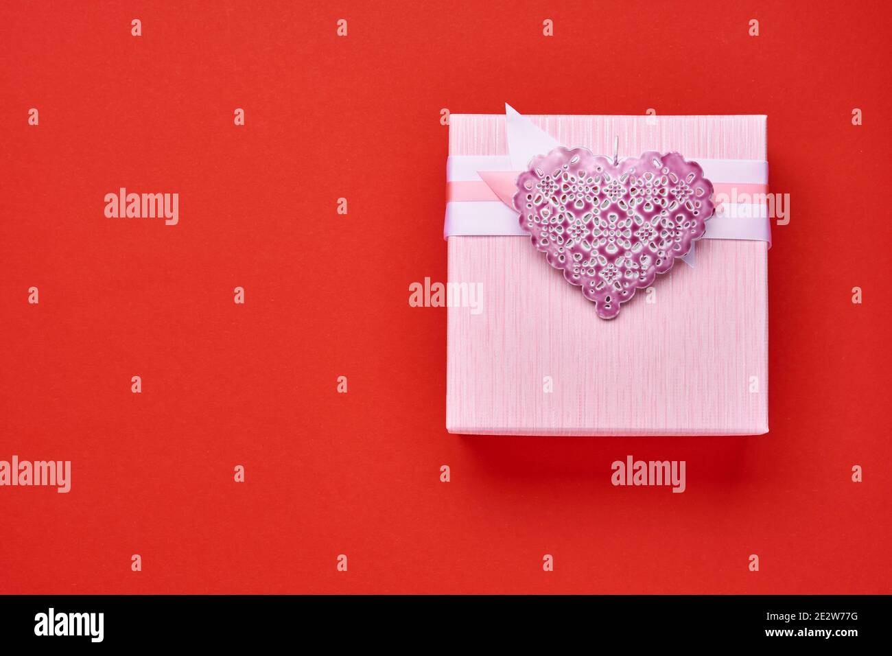 Square pink gift box with ribbon and heart on red background ...