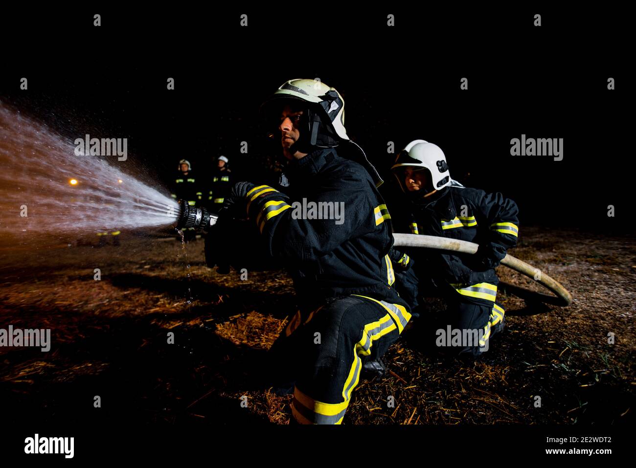 Firemen in uniform fighting a burning fire during emergency situation ...