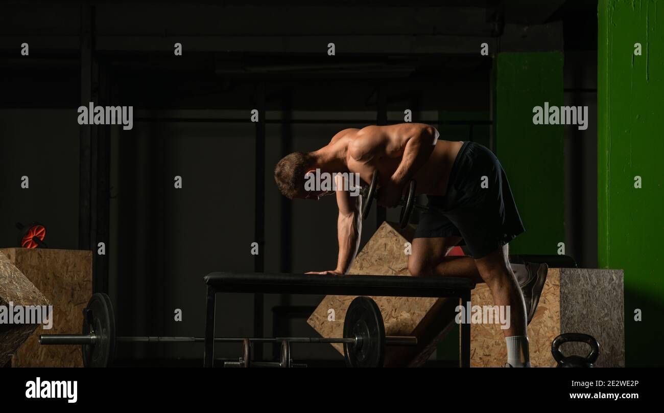 Good looking young man doing triceps dumbbell kickback exercises with ...