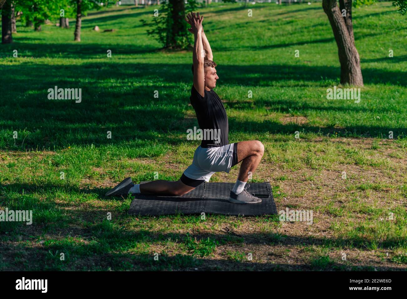 Sporty young man stretching legs and doing forward lunge while having ...