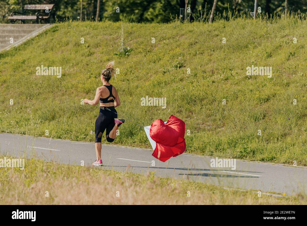 Side view of a young fitness woman running using red resistance ...