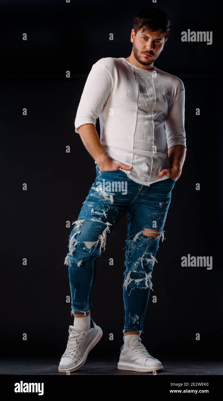 Attractive young male model posing in denim pants over black wall Stock ...