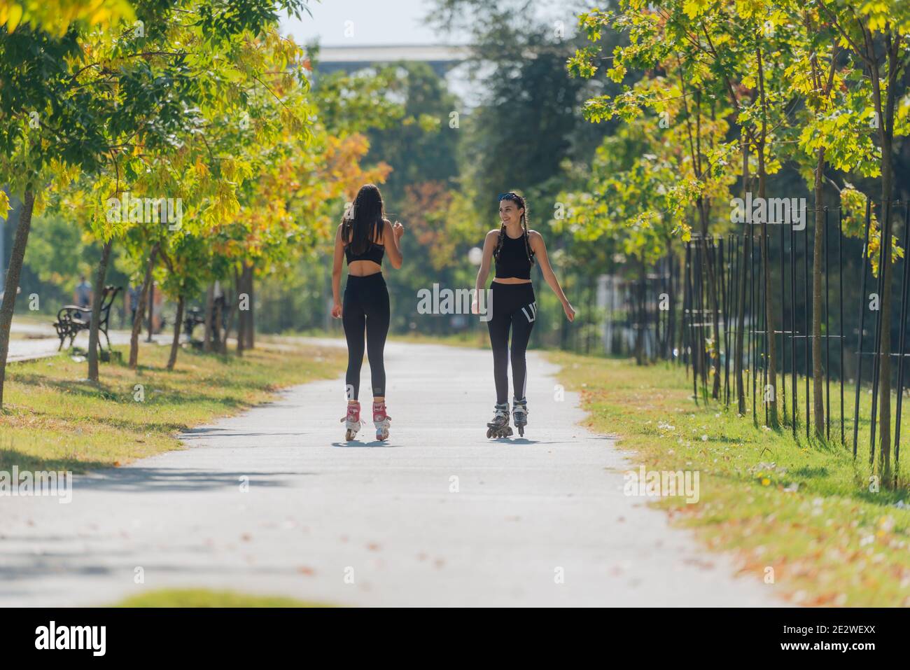 Rearview of two young fit women on roller skates riding outdoors on ...