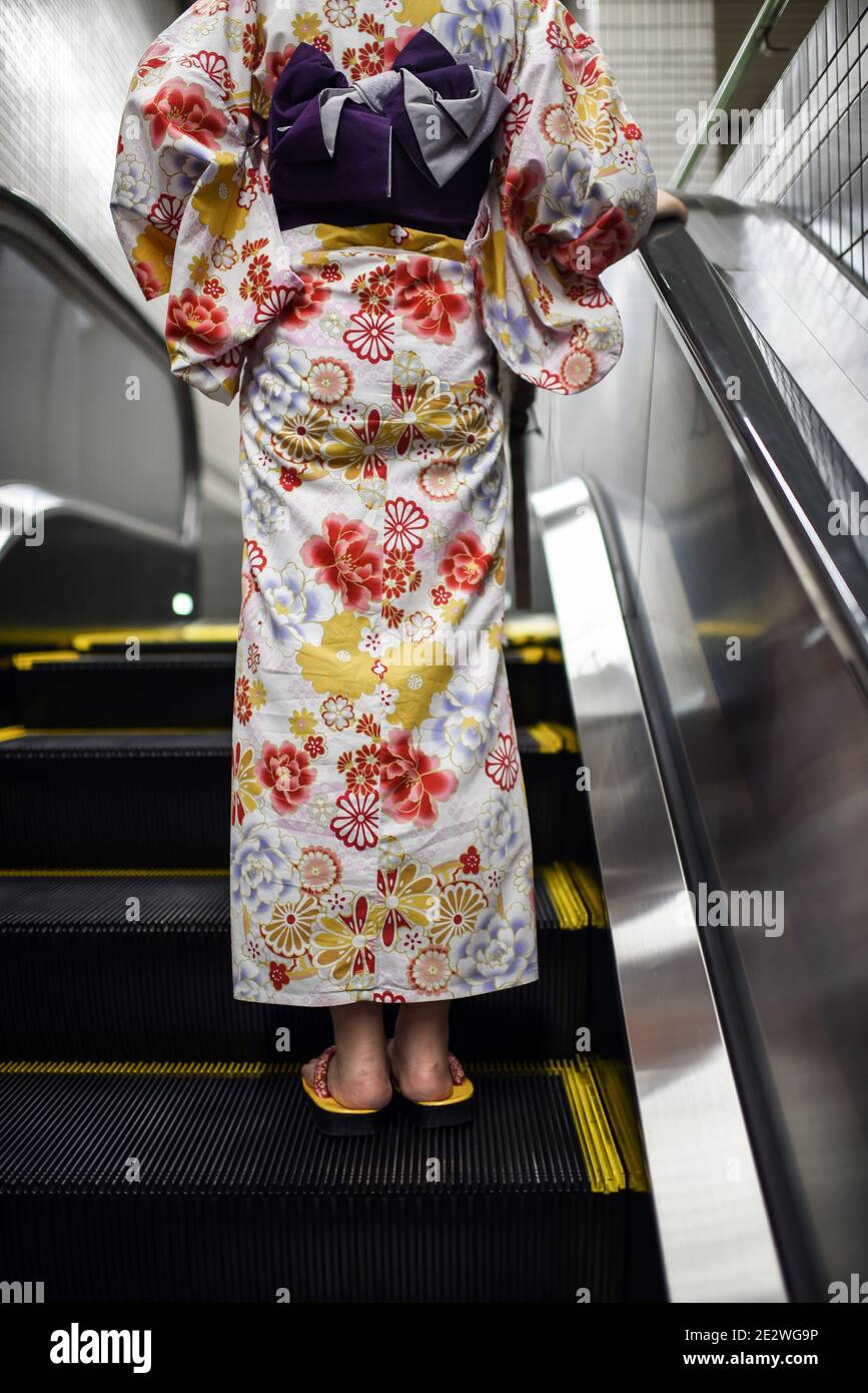 Young Woman Wearing A Japanese Kimono And Geta Shoes In Escalator Of