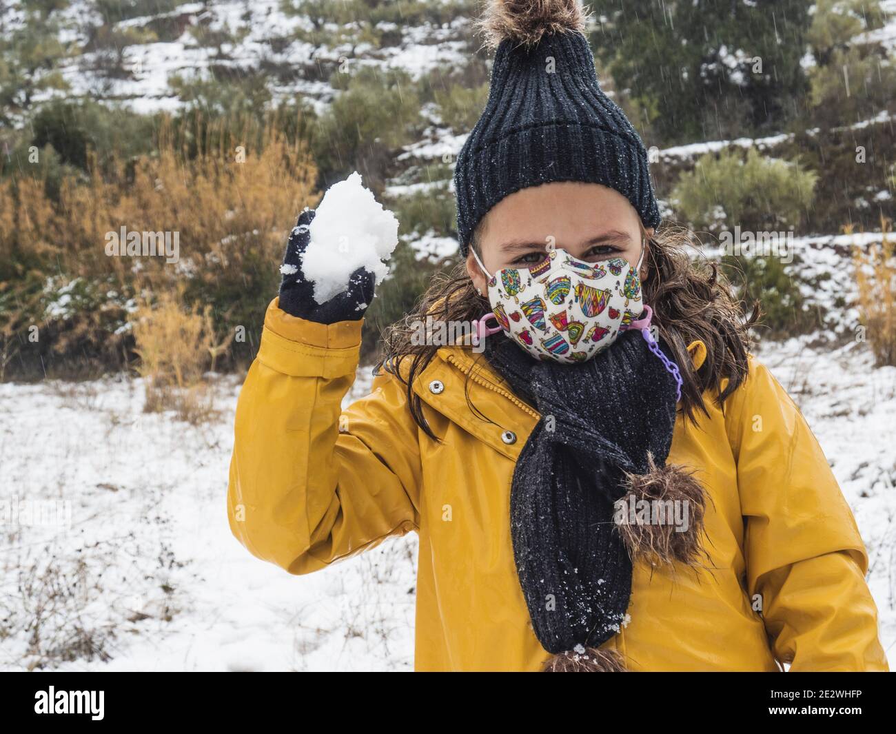Caucasian girl with a face mask making a snowball Stock Photo - Alamy