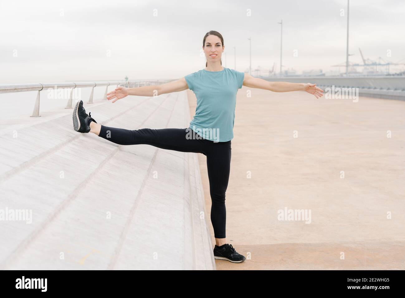 Girl practicing side stretch, open arms, yoga posture, on the street ...