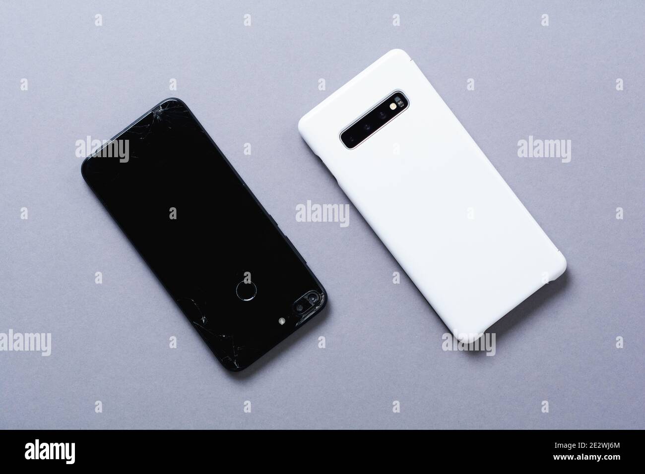 Old broken black and new white smartphones on gray background. The ...