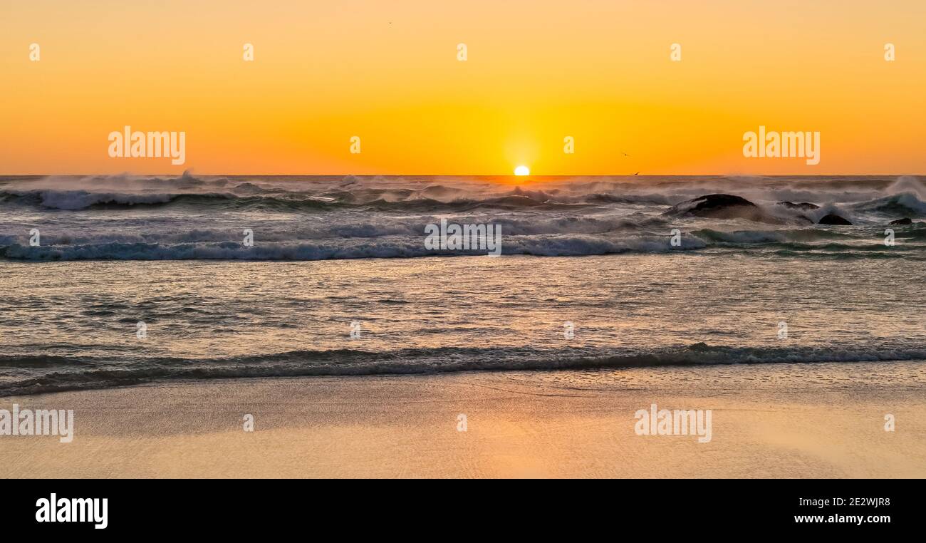 Orange and yellow shaded sunset above the wavy waters seen through a ...