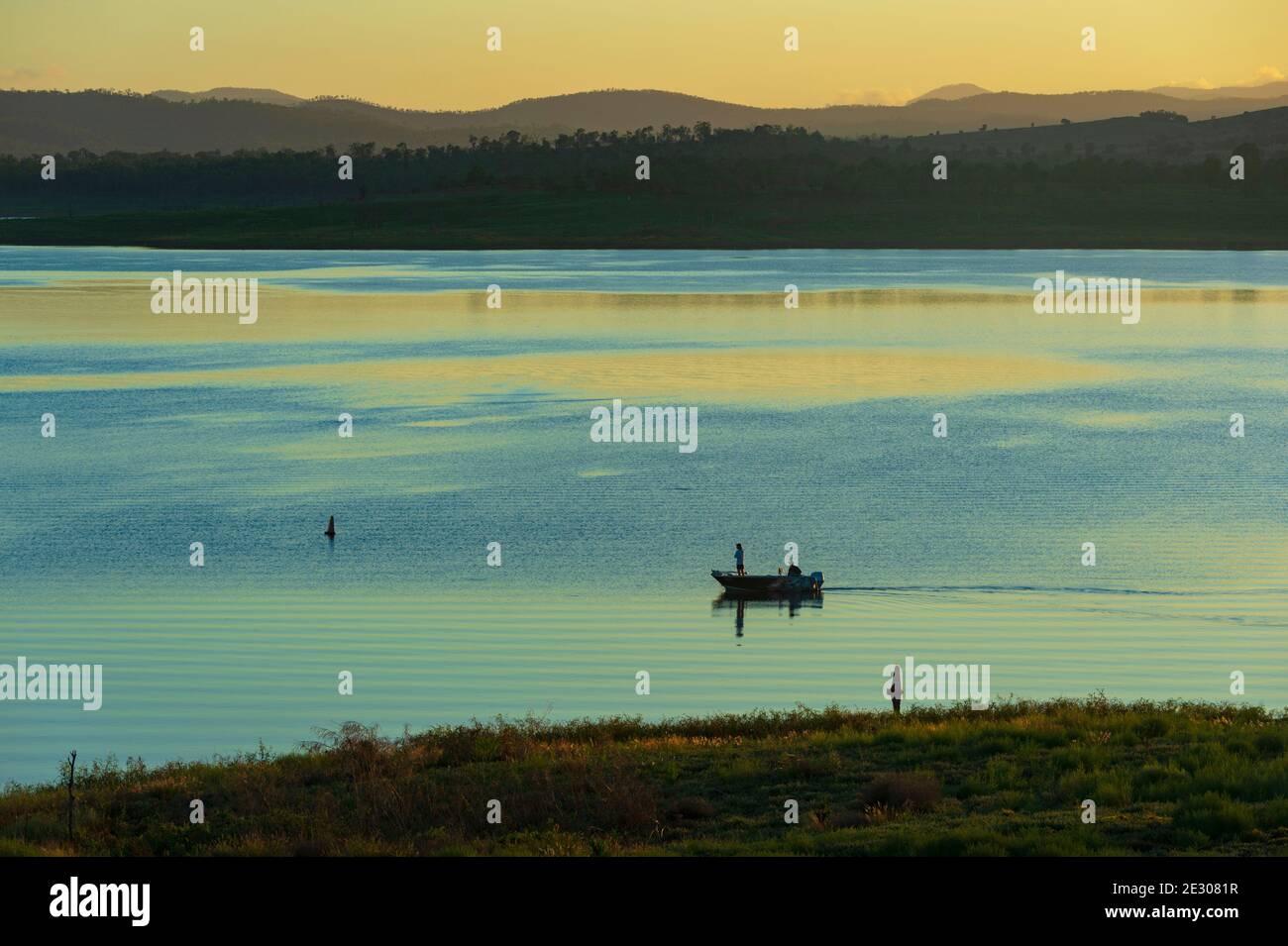 Silhouettes of fishermen fishing from a boat on Lake Callide at sunrise ...