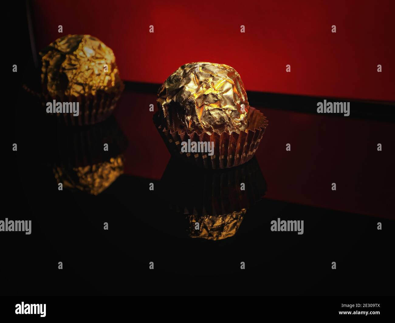 Round candies in golden foil on a black and red background. Wrapped ...