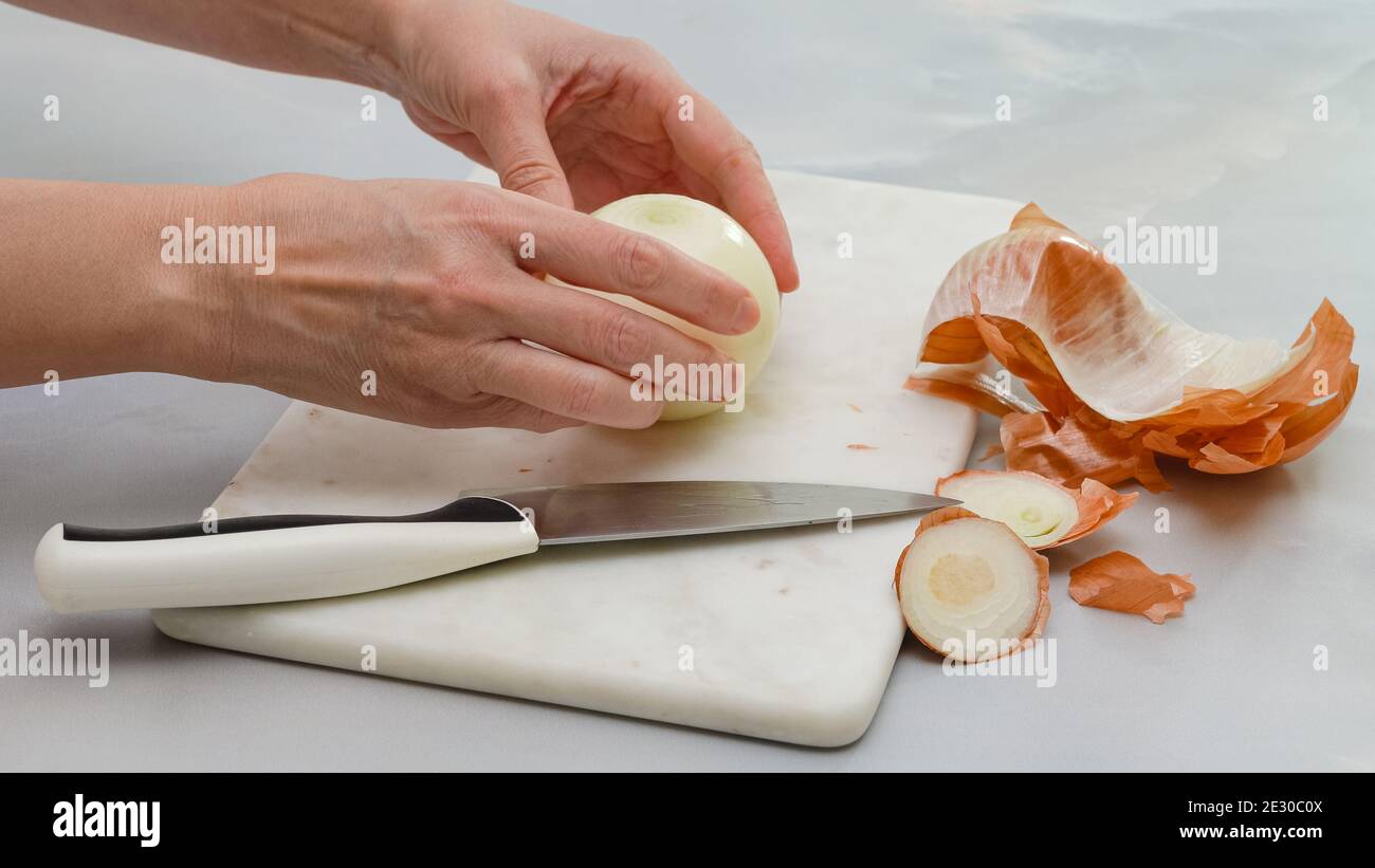 Peeling white onion on marble cutting board. Close up cooking process ...