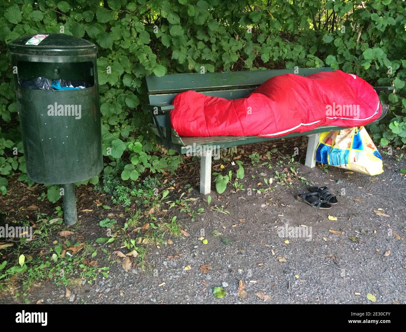 a person sleeping on a park bench in a hiking sleeping red bag ...