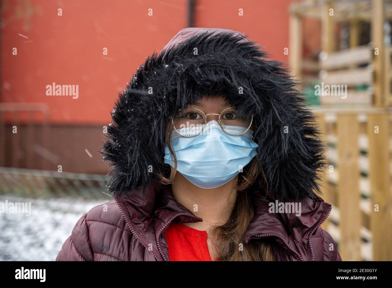 A teenage girl with in a winter jacket with a hood wearing a protective ...