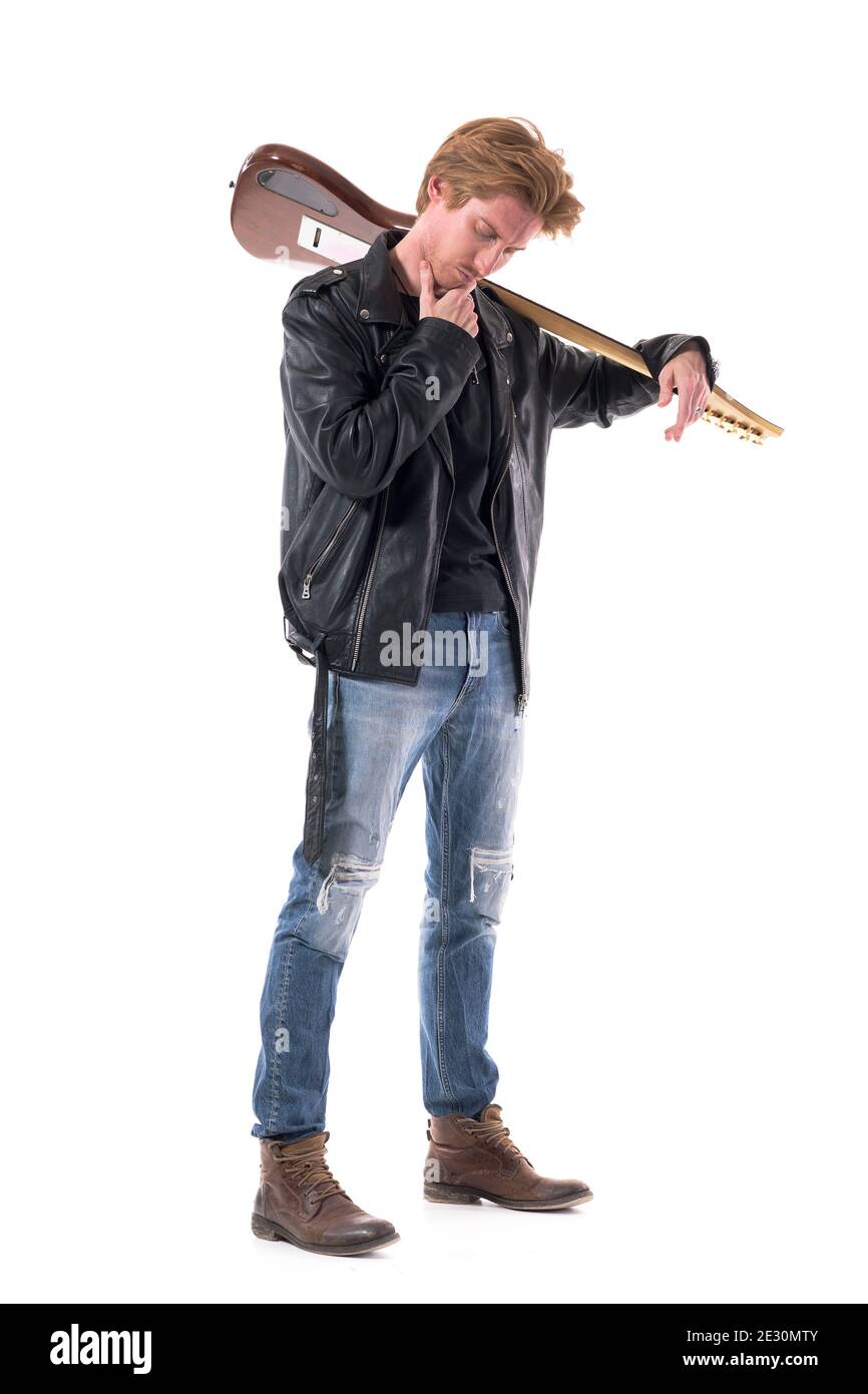 Thoughtful young man guitarist carrying guitar on shoulder looking down ...