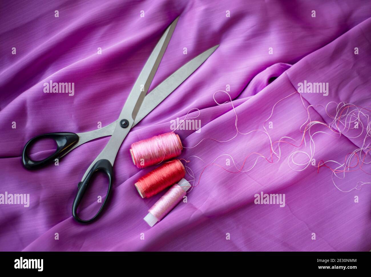 Pink textile silk background with spools of thread and with scissors ...