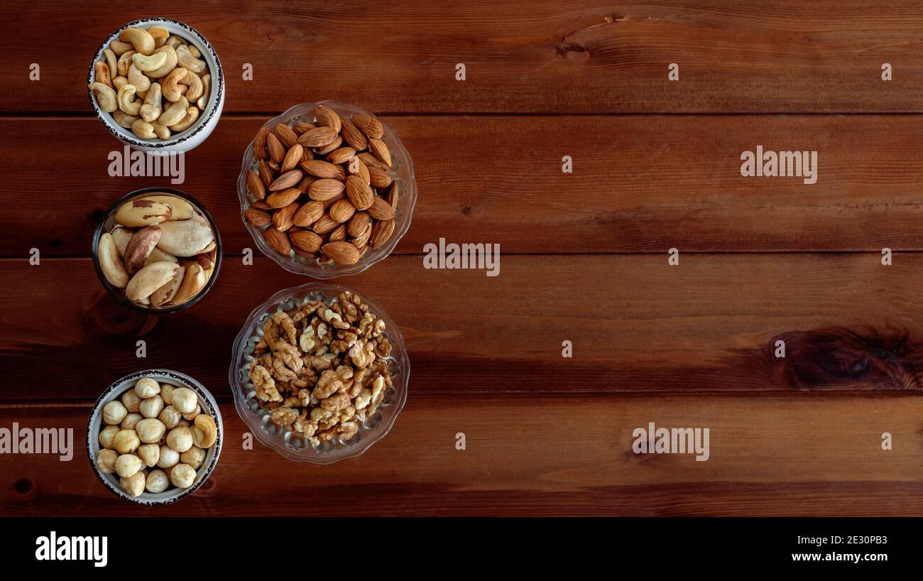 Mixed nuts in different bowls on wooden table. Top view with place for ...