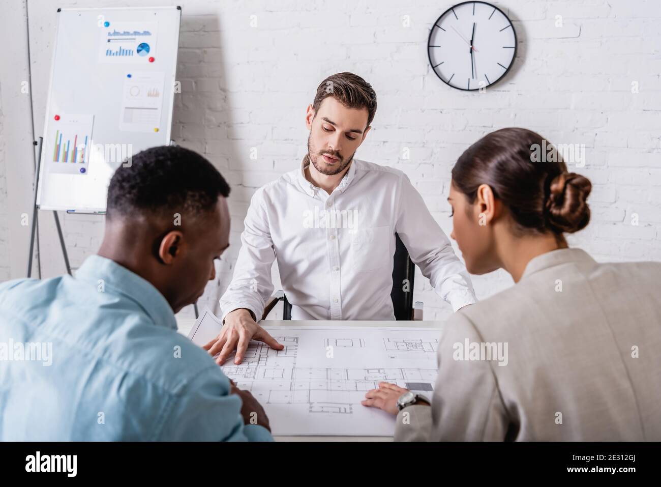 multicultural businesspeople looking at blueprint near interpreter and ...