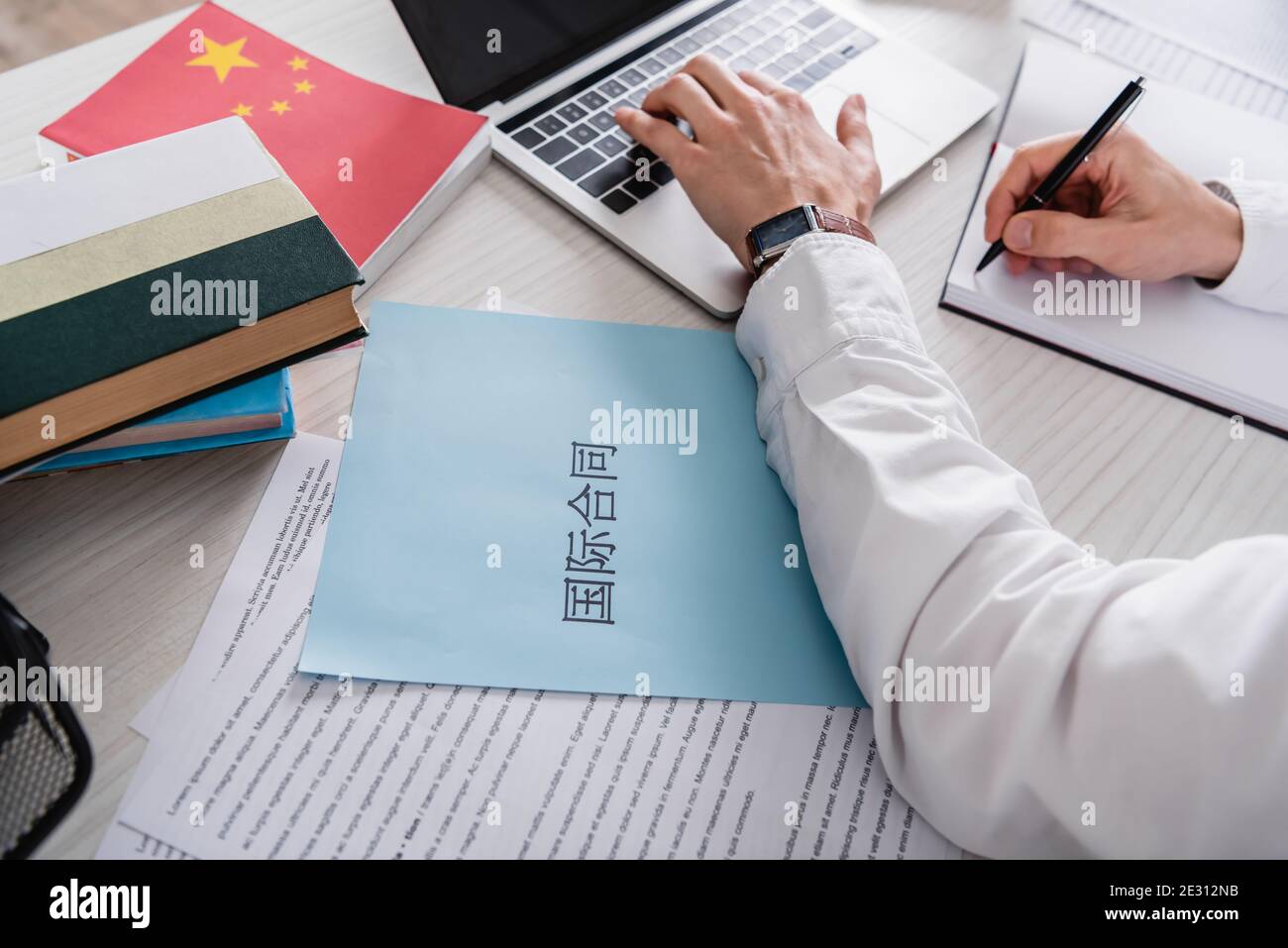 partial view of translator writing in notebook and typing on laptop ...