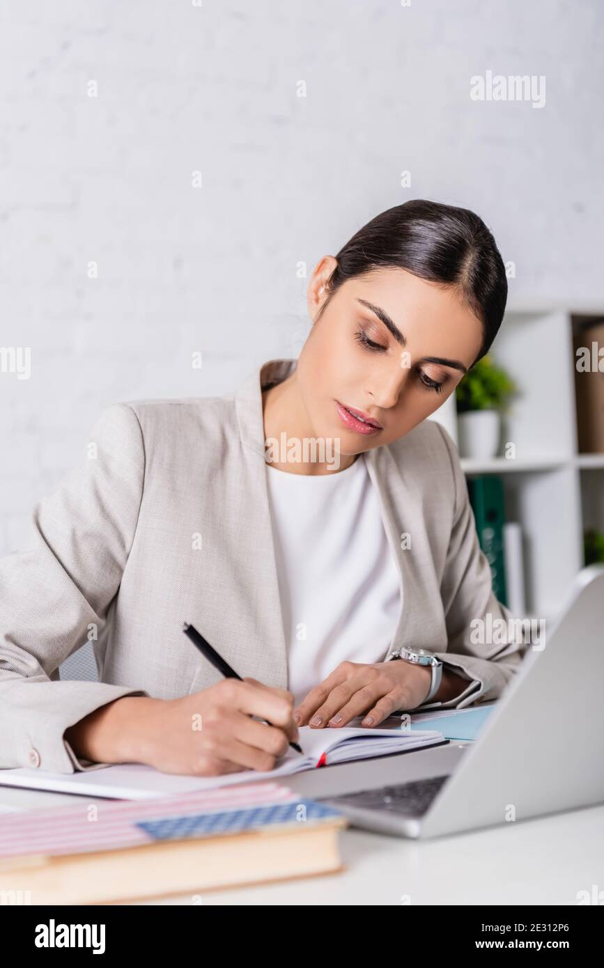 translator writing in notebook near laptop and english dictionary on ...