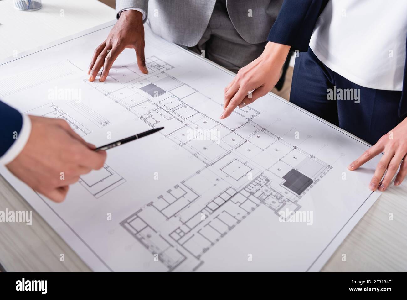 partial view of interracial business partners pointing at blueprint ...