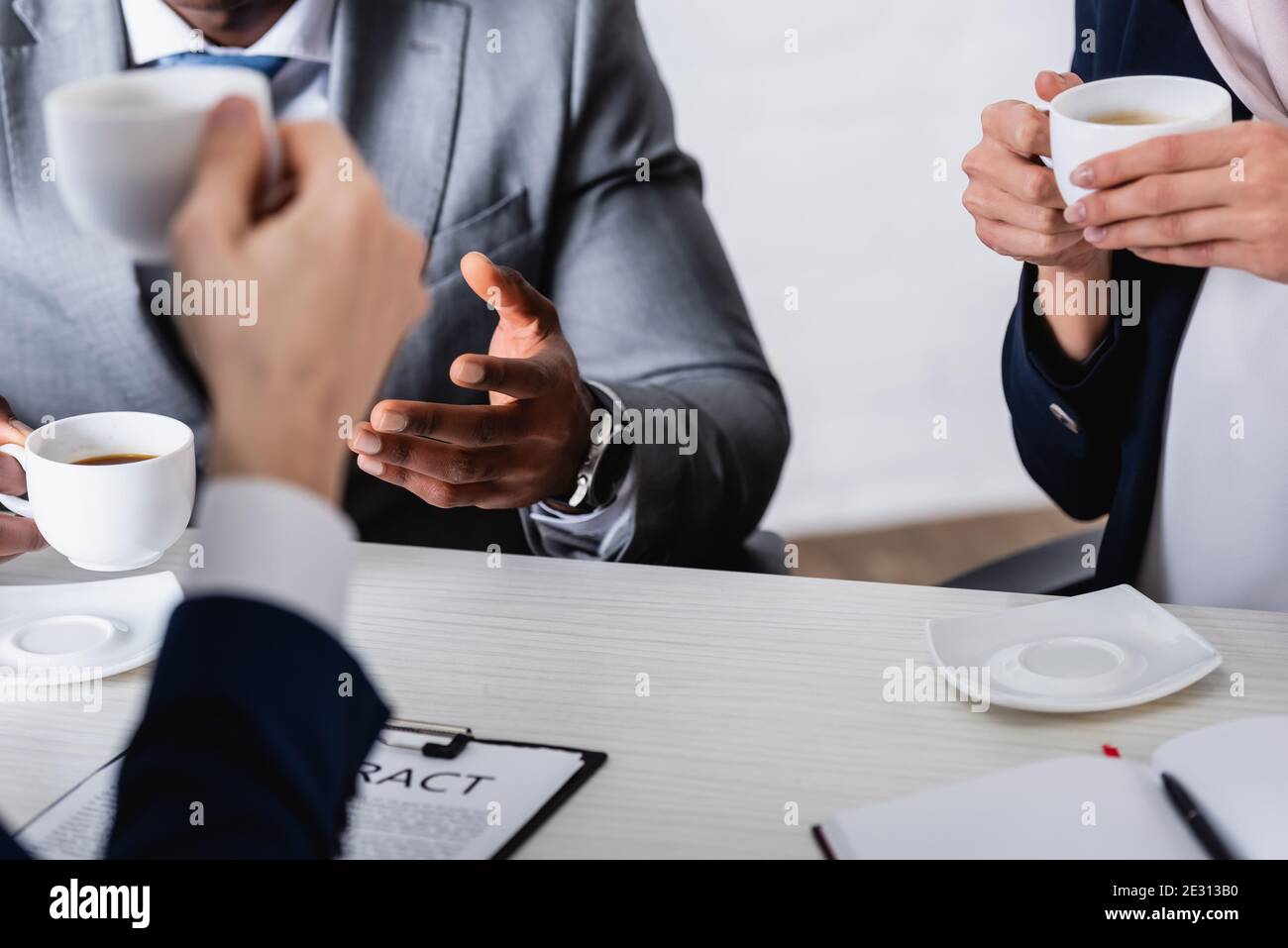 selective focus of multiethnic business partners holding cups during ...