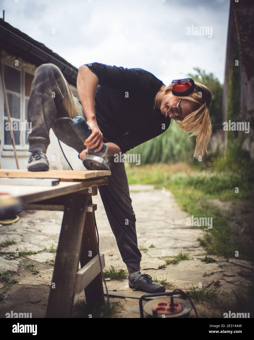 A woman sanding a piece of wood using a sander while wearing ear ...