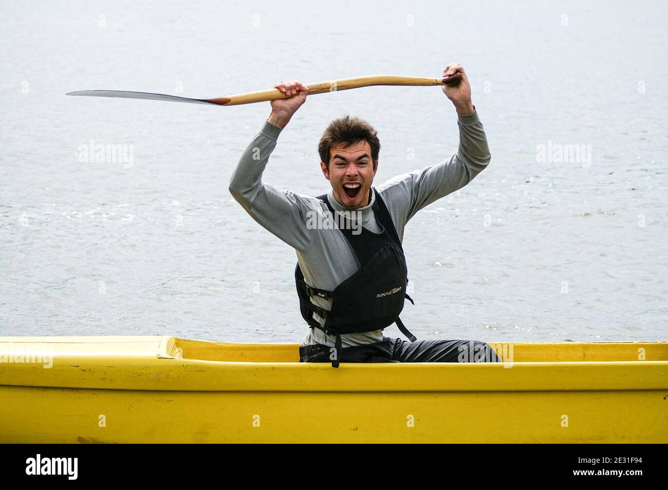 A man holding a canoe paddle above his head and cheering after winning ...