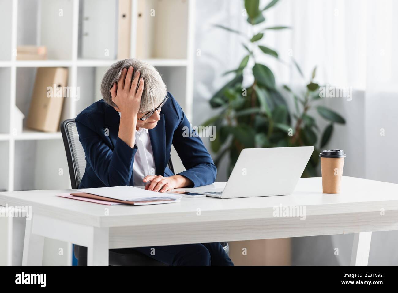 tired team leader in glasses looking at laptop on desk in modern office ...