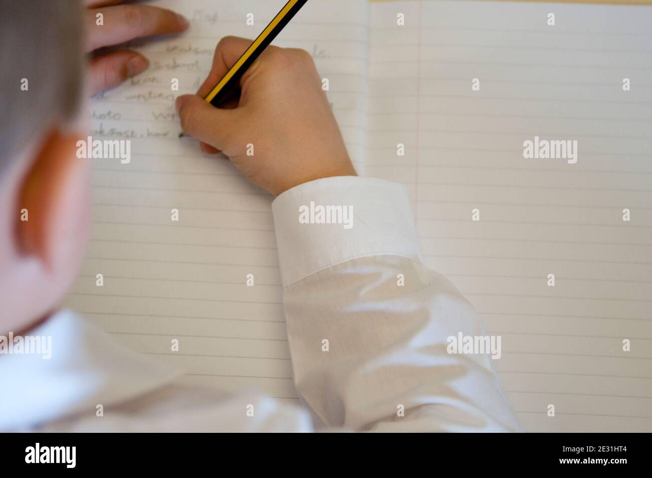 School boy writing on lined paper at his desk Stock Photo - Alamy