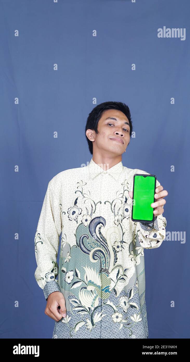 asian man with batik clothes and pointing at green screen cellphone ...