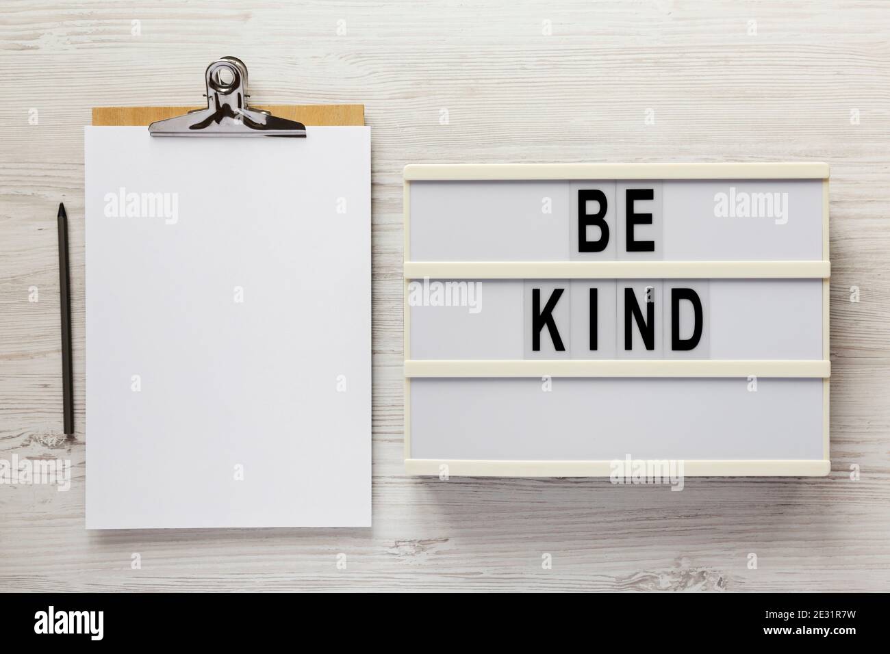 'Be kind' on a lightbox, clipboard with blank sheet of paper on a white ...