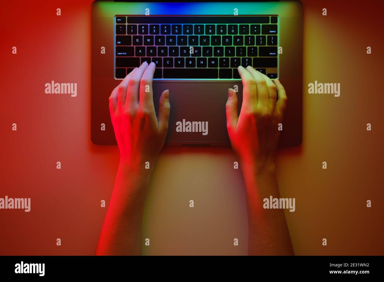 Hands on a modern laptop keyboard, top view and bright lit red ...