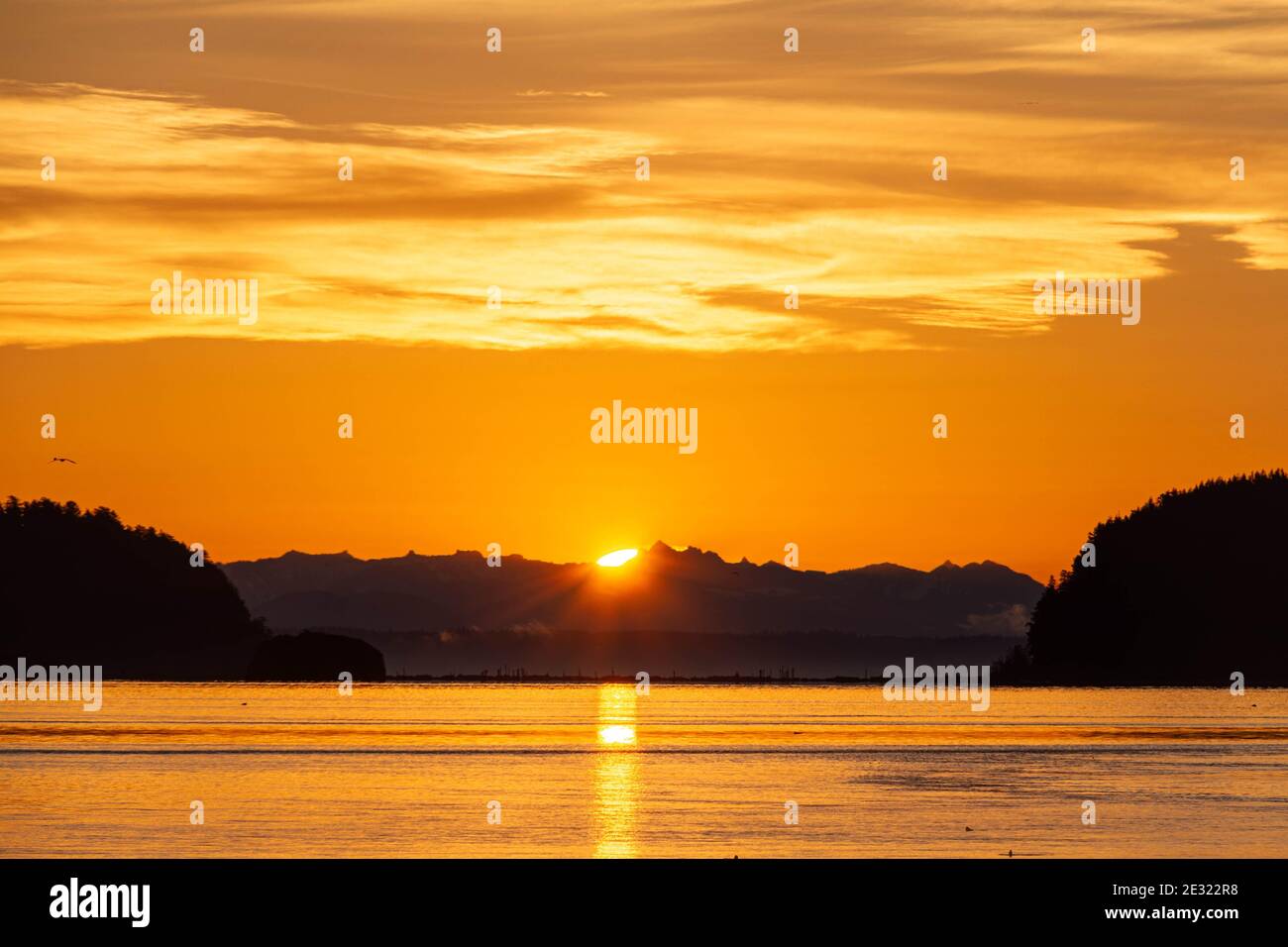 Dramatic sun rising between two hills with water in the foreground ...