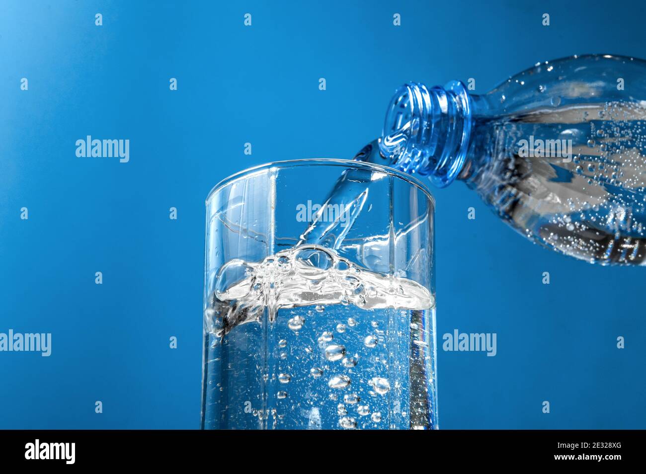 Pouring water from plastic bottle into glass on blue background. Stream ...