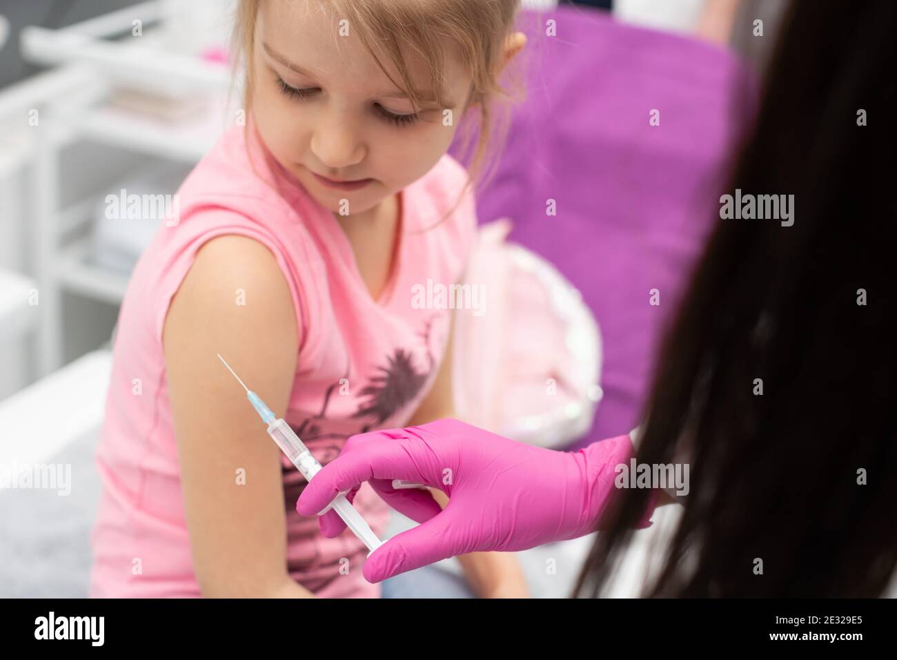 The nurse gently inserts the needle into the little girl's arm. The ...