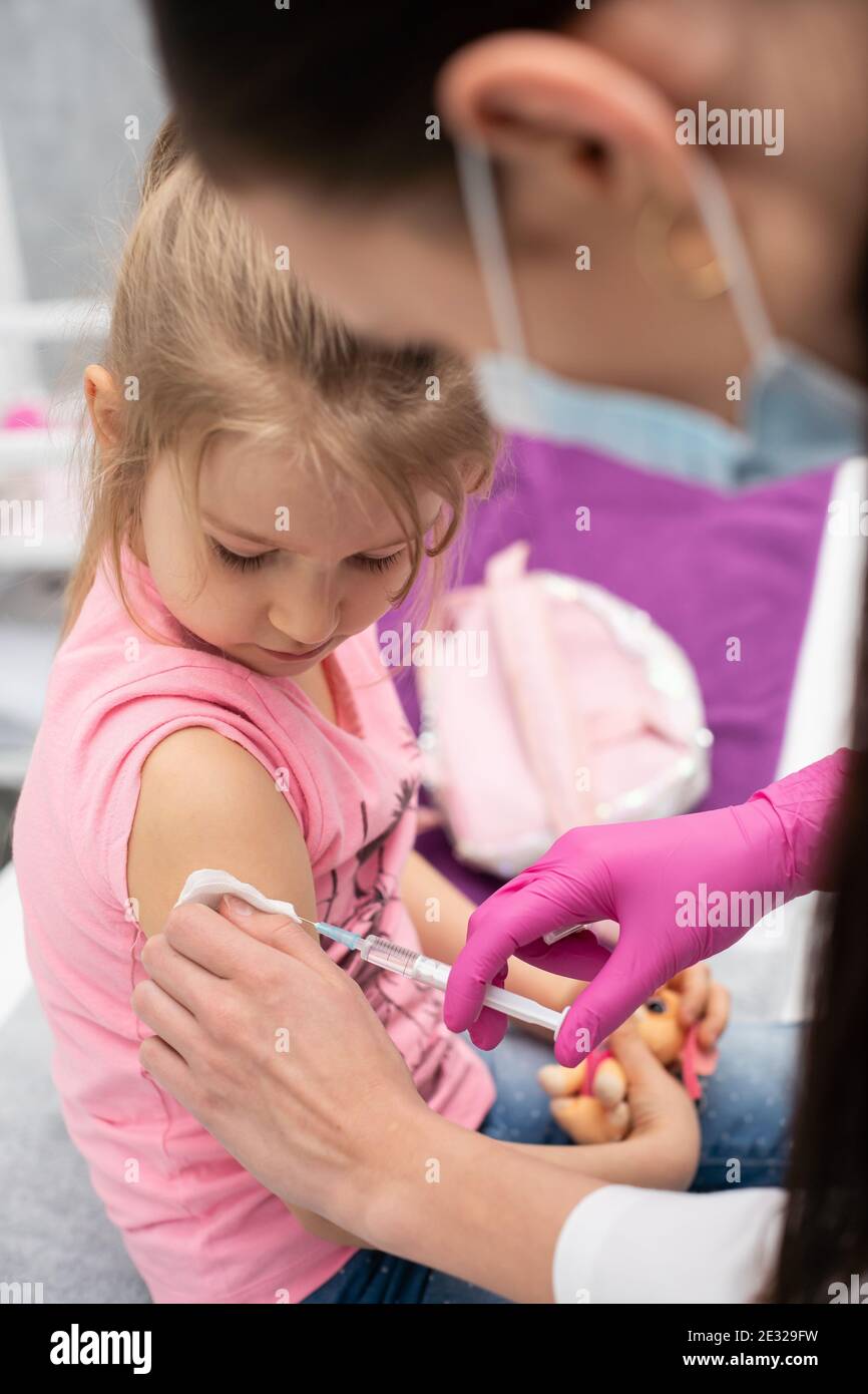 The nurse gently inserts the needle into the little girl's arm. The ...