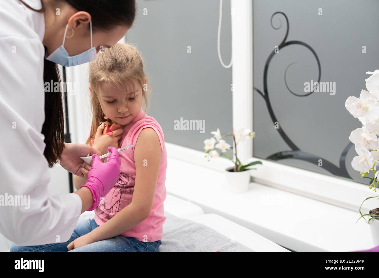 The nurse gently inserts the needle into the little girl's arm. The ...