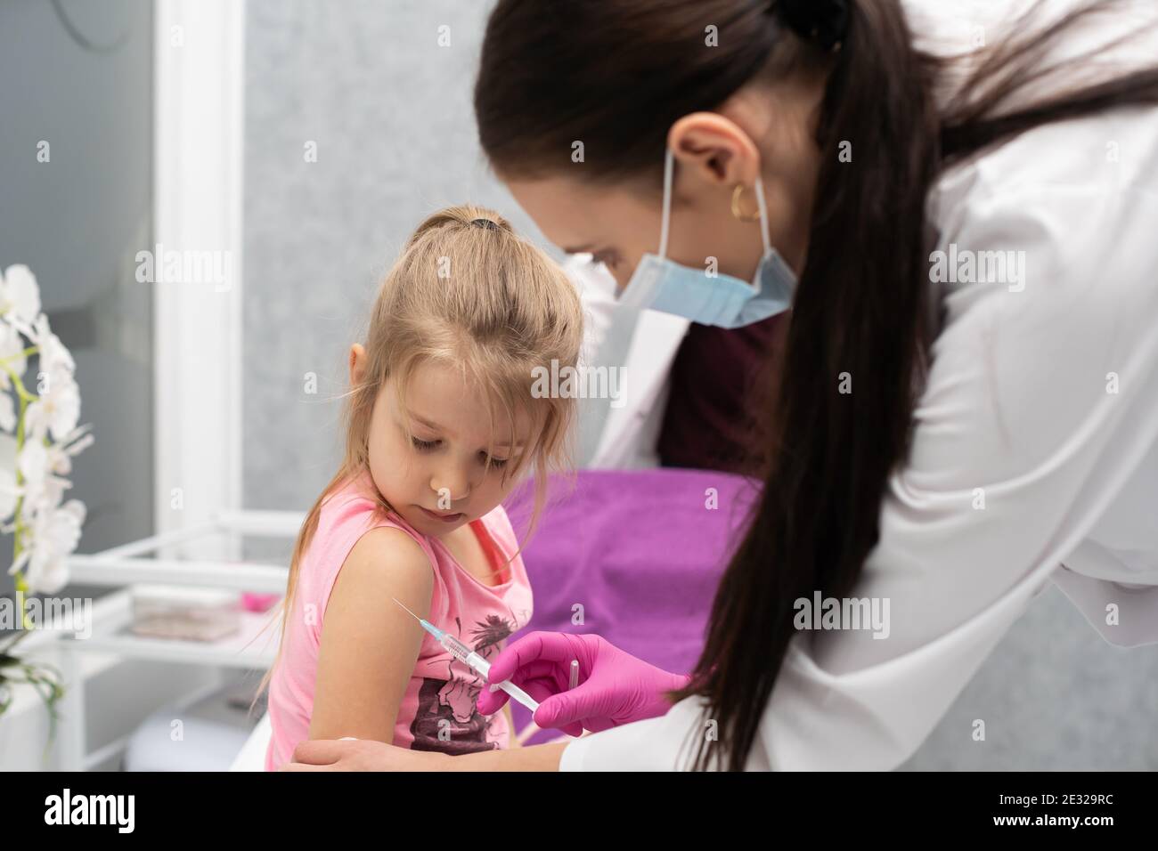 The nurse gently inserts the needle into the little girl's arm. The ...