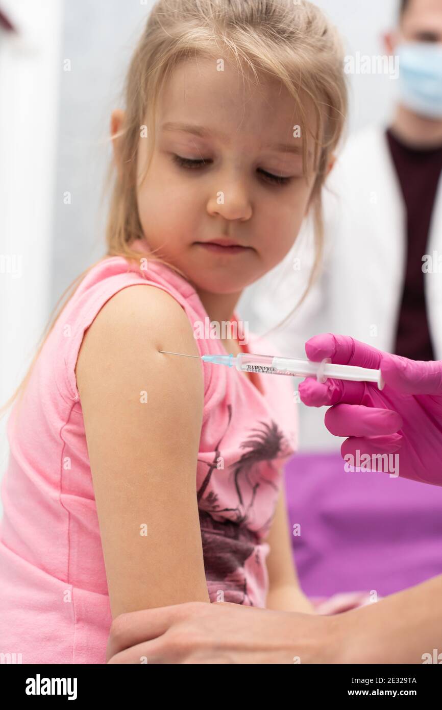 The nurse gently inserts the needle into the little girl's arm. The ...